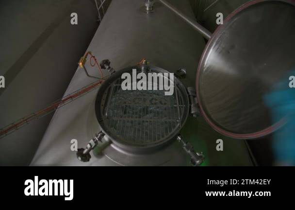Worker opens hatch in metal tank with chemical materials in plant ...