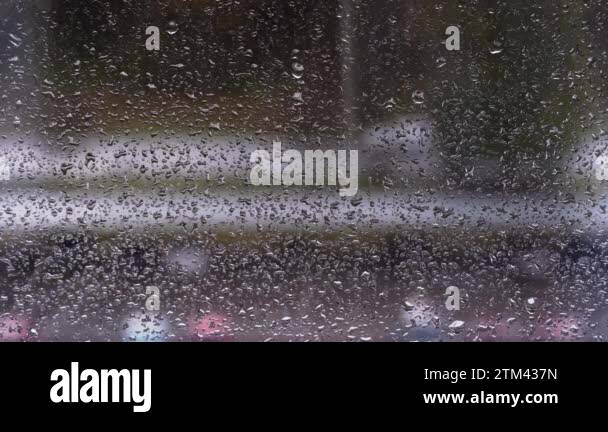 Drops of rain flow down the glass against the backdrop of moving cars ...