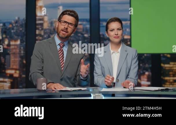 Smiling anchors talking news to audience at evening chromakey tv studio ...
