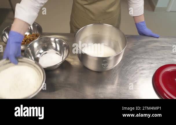 A close-up of an expert chef adding flour to a metallic mixer bowl to ...