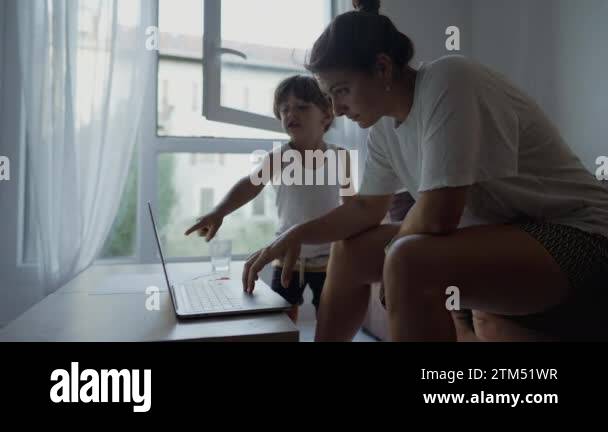 Mother and child in front of laptop screen at home. Son pointing at computer. Candid parent ...