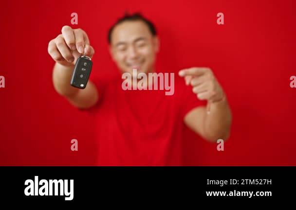 Overjoyed young chinese man excitedly pointing to keys of his new car ...