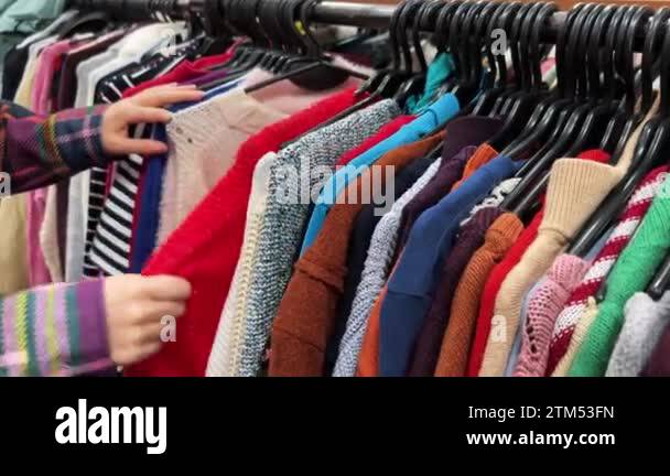 A young buys clothes in a second-hand shop. Thrift store hangers with ...