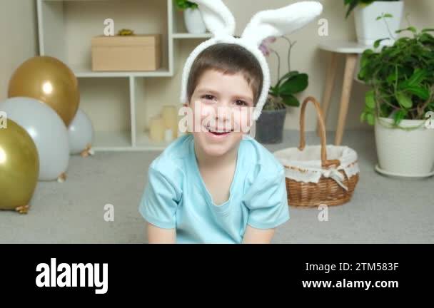 A 5 or 6 year old preschool boy with rabbit ears on his head smiles ...