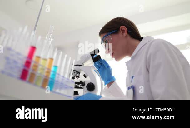 Scientist examines test tubes with various liquids and looks through ...