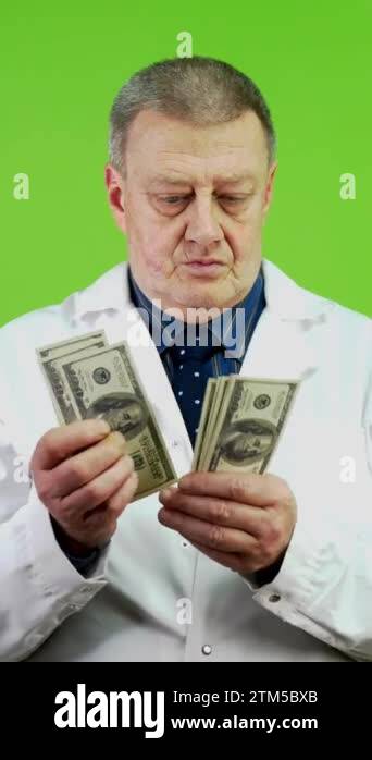 Senior doctor counts money dollars in hands for medical services or ...