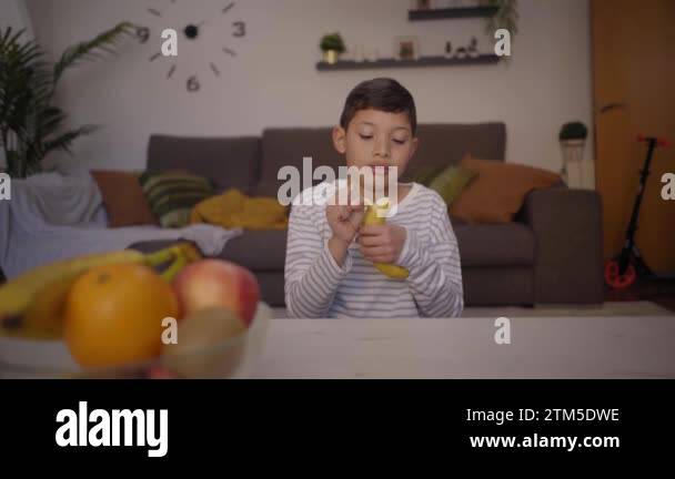 Latin little boy quietly snacking on banana sitting in living room ...