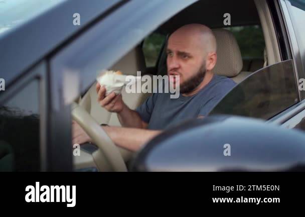 Emotional millennial man driving a car, eating burger, had an accident ...
