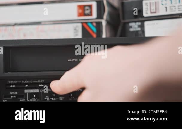 Male hand inserts VHS cassette into a VCR Video recorder. Black vintage ...