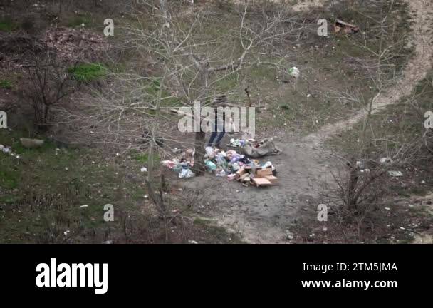 Homeless person sorts garbage next to a large pile of waste. A homeless ...