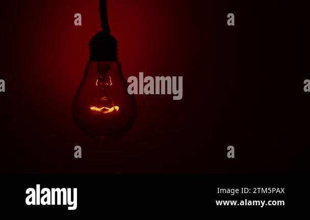 Light bulb lights up and goes out on a red background in the dark. Slow ...