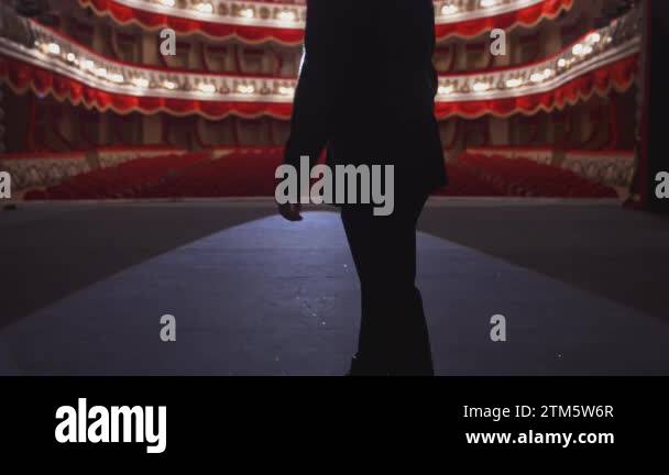 Man with microphone on theatre stage. Male actor in elegant suit walks ...