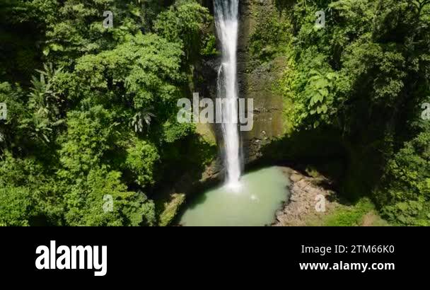 Rainbow over single layer cascade of water surrounded by greenery trees and plants. Alalum Falls ...