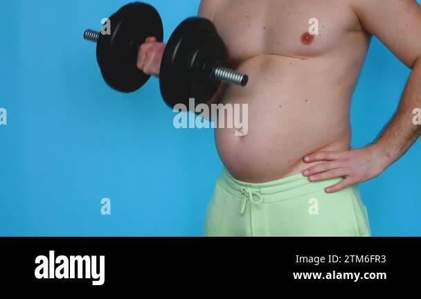A fat man does an exercise with dumbbells for two hands on a blue ...