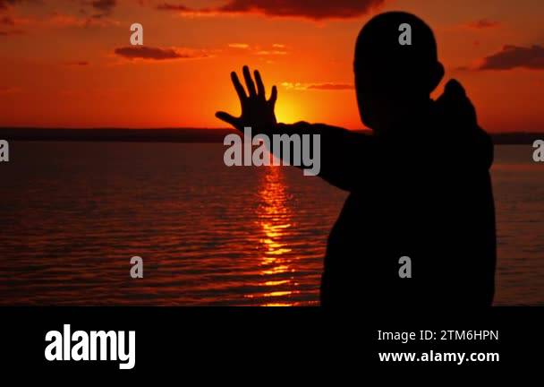Man reaches out with her hand towards the setting sun in silhouette ...