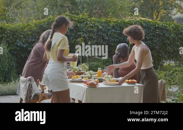 Modern ethnically diverse family setting table for dinner in backyard ...
