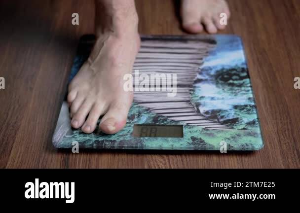 Male on the Scales Measures the Weight. Close up. A man barefoot steps ...
