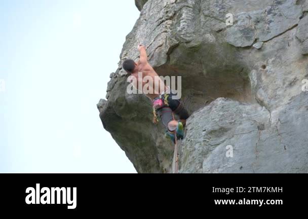 Young man climbing steep wall of rocky mountain. Male climber overcomes ...