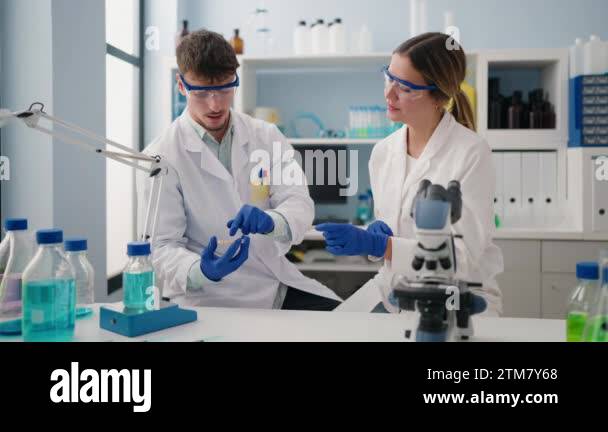 Young couple wearing scientist uniform using microscope working at ...