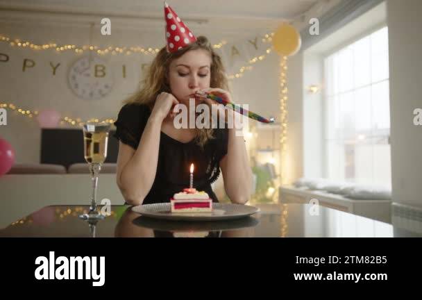 A woman with a party cap blowing a candle on a birthday cake with ...