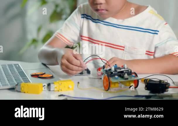 Asian kid boy plugging energy and signal cable to sensor chip with Arduino robot car, Little ...