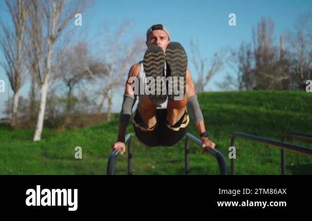 Man flexing abs on parallel bars in outdoor gym. Working on his core. Full length shot muscular ...