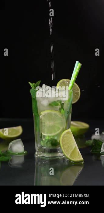 A Pouring Stream of Water into a glass of Mojito against a black background. Refreshing Mojito ...