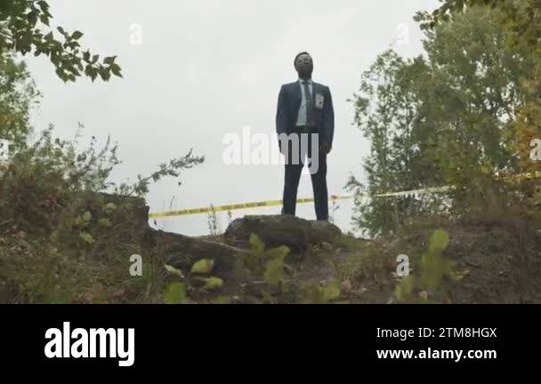 Low angle full length shot of pensive young Black male detective in ...