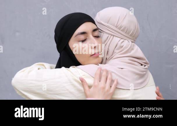 Two Muslim women in black and white hijabs enclose each other in a warm ...