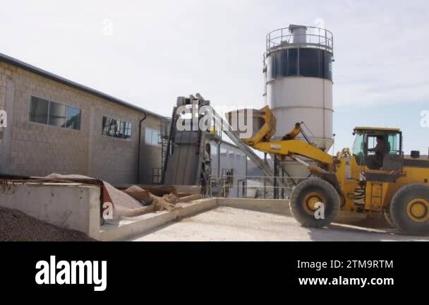 At a cement factory, a yellow industrial crane unloads sand and gravel ...