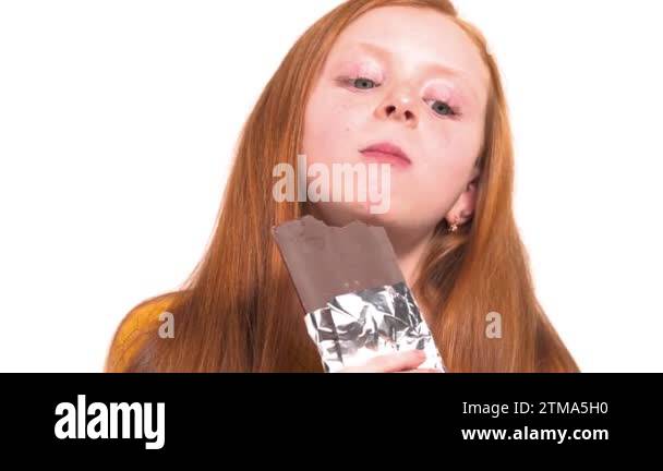 Close-up of foxy haired girl with green eyes biting a huge block of ...