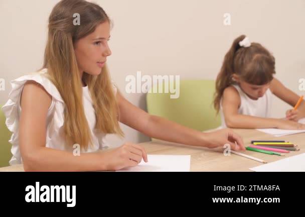A side view of lovely girls drawing with colored pencils during ...