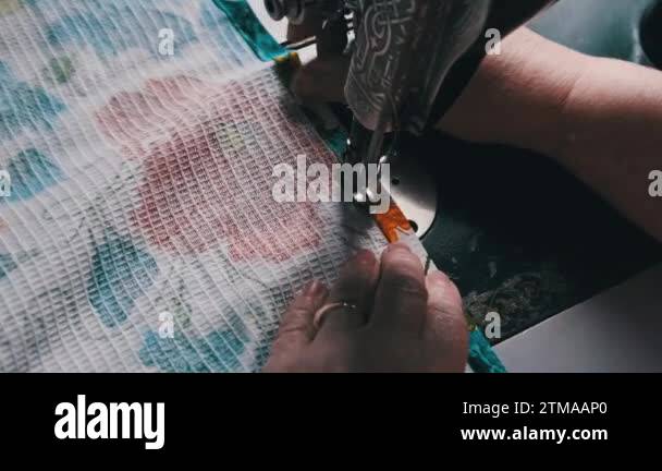 An aged seamstress sews at a traditional sewing machine at home in slow ...