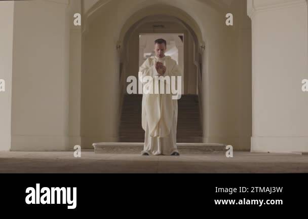 Full length slowmo of priest in long white robe standing between two ...