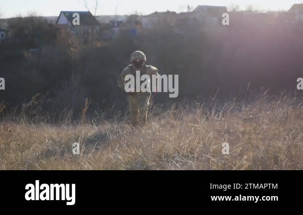 Young male military in uniform jogging among dry grass at countryside ...