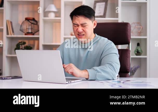 Sick Japanese office worker working on laptop in office, experiences ...