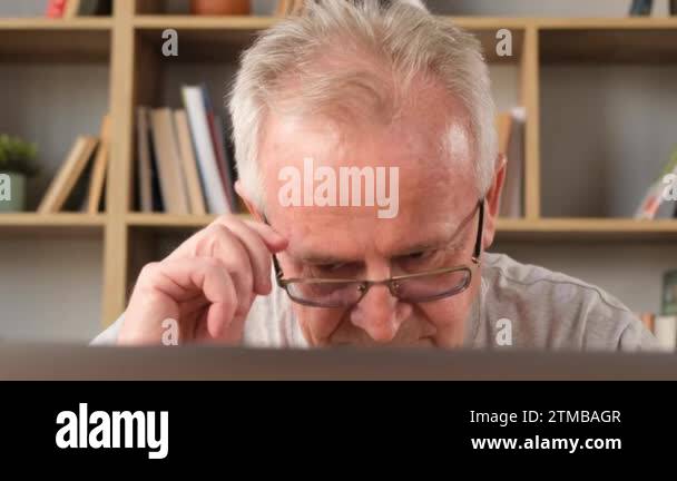 Old gray-haired concentrated pensioner looking at laptop monitor and ...
