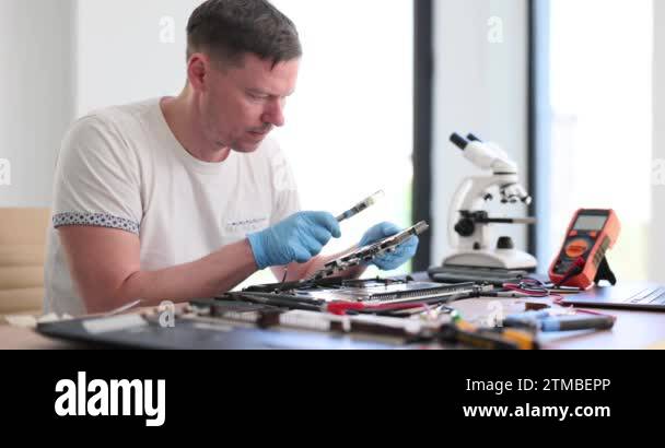 Male person in rubber gloves looks at printed circuit board of laptop ...