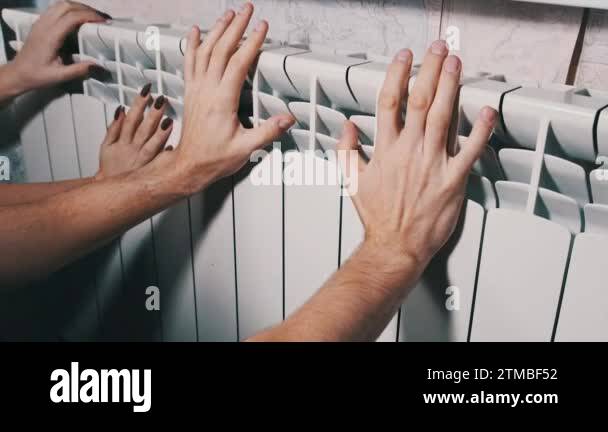 Frozen male and female hands touch the home radiator and try to warm up ...
