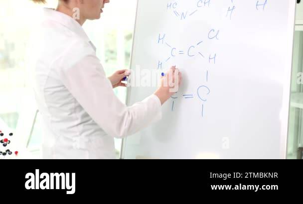 Focused woman writes chemical formulas on whiteboard with blue marker ...