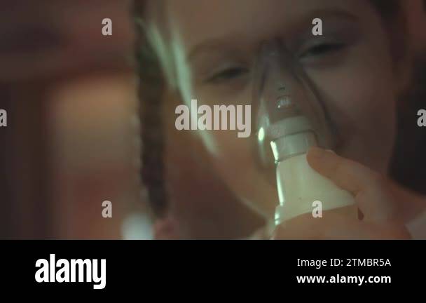 Beautiful little girl makes inhalation using a compressor inhaler while ...