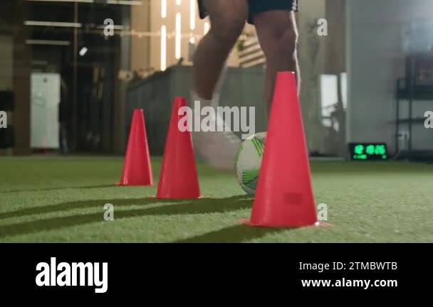 Unrecognizable footballer running dribbling ball between cones in sport ...
