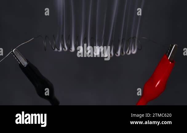 Nichrome wire heats up to red with smoke under a high electric current ...