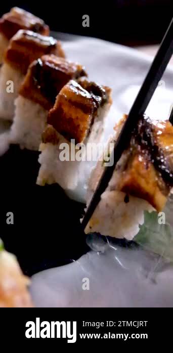 closeup of black chinese chopsticks take eel sushi from plate with cold ...