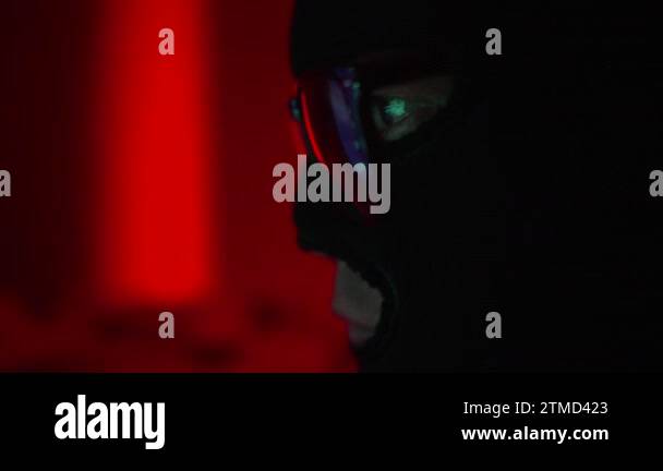 Man hacker programmer in a black mask hacks the system on a computer, a code with a ticker is ...