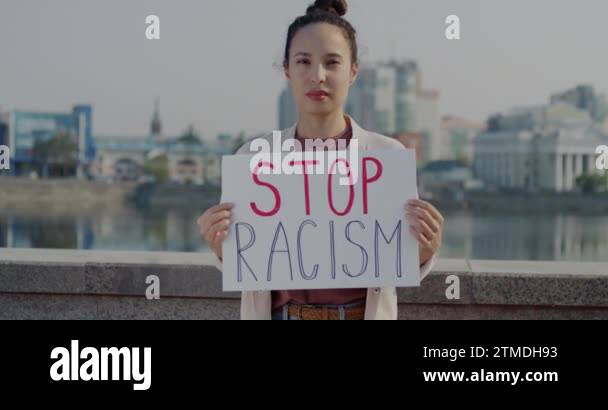 Slow motion portrait of young biracial woman holding Stop Racism banner ...