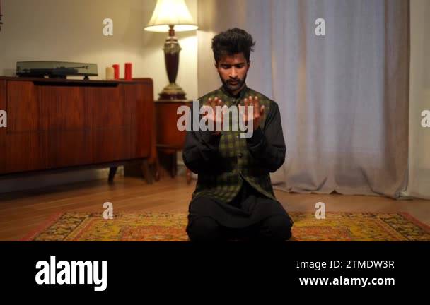 Wide shot concentrated Muslim man praying on knees in living room as ...