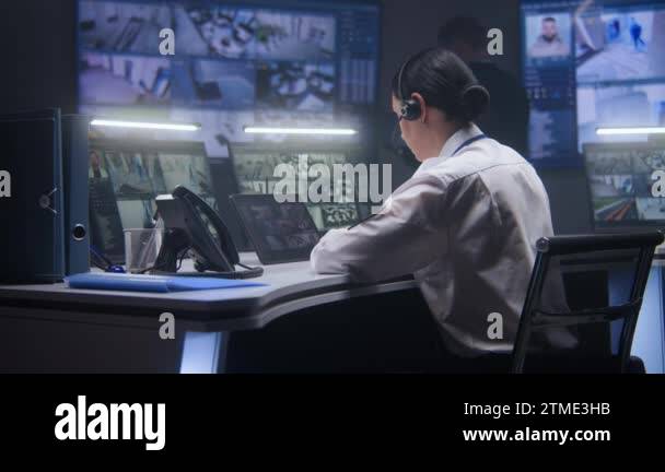 Female security officer in headset zooms and controls CCTV cameras ...