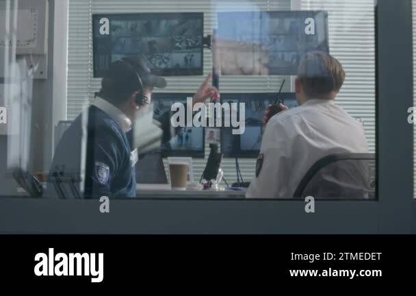 Security officers sit in surveillance room and monitor CCTV cameras with AI scanning system on ...