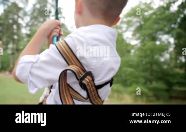 Cheerful laughing boy riding on the zip-line strung between two trees ...
